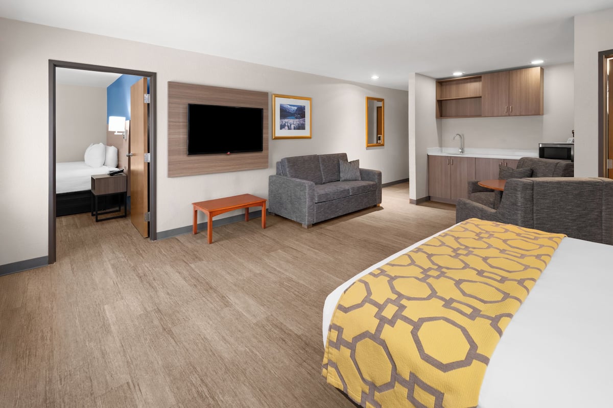 Quarto de hotel com cama, dois sofás, televisão, mesa pequena, área de cozinha e banheiro.