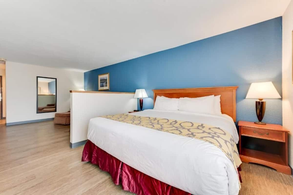 Quarto de hotel com uma cama, duas mesas de cabeceira, um criado-mudo, um espelho e uma parede com um quadro.