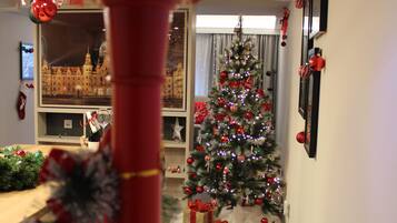 Um quarto com árvore de Natal decorada com enfeites vermelhos e verdes, um quadro pendurado na parede e uma garrafa de champanhe sobre uma mesa.