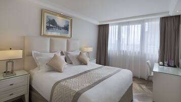 Quarto de hotel com uma cama grande, mesas de cabeceira com abajures, uma escrivaninha e uma cadeira.