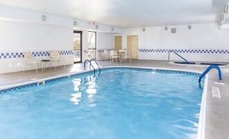 Uma piscina interna com água azul cristalina, borda em azulejo e alguns cadeiras de praia e mesas no deck.