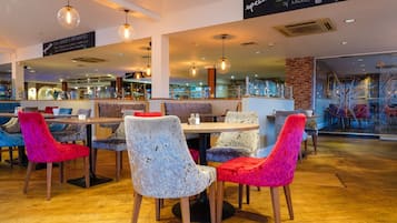 Um restaurante moderno com piso de madeira, mesas redondas e cadeiras coloridas.