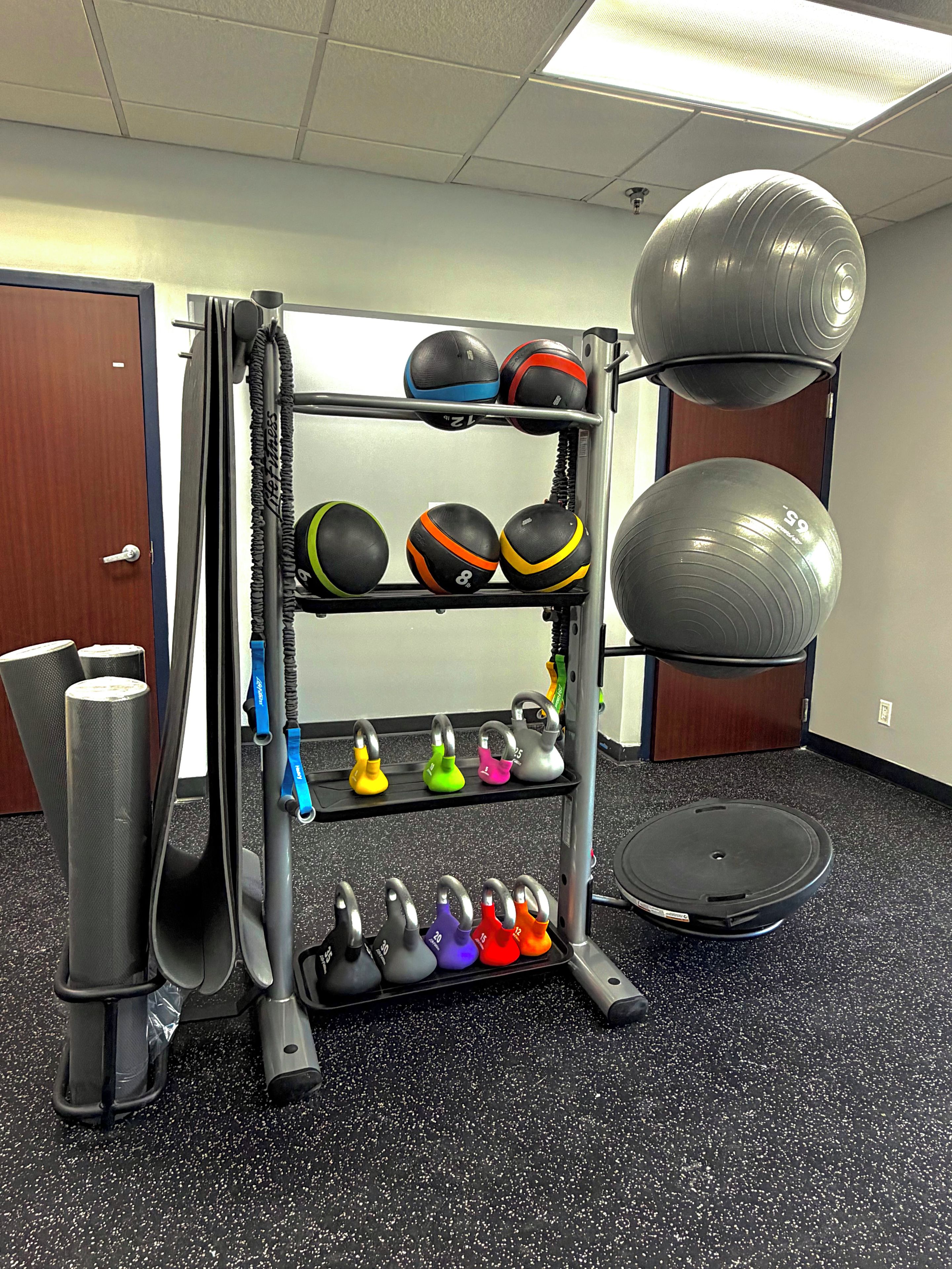 Uma academia com um suporte de kettlebells, bolas de medicina e uma bicicleta ergométrica.