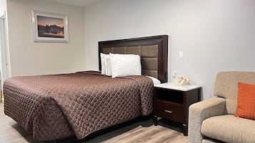 Quarto de hotel com cama, mesa de cabeceira, cadeira e quadro na parede.