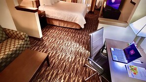 Quarto de hotel com cama, escrivaninha, laptop e televisão.