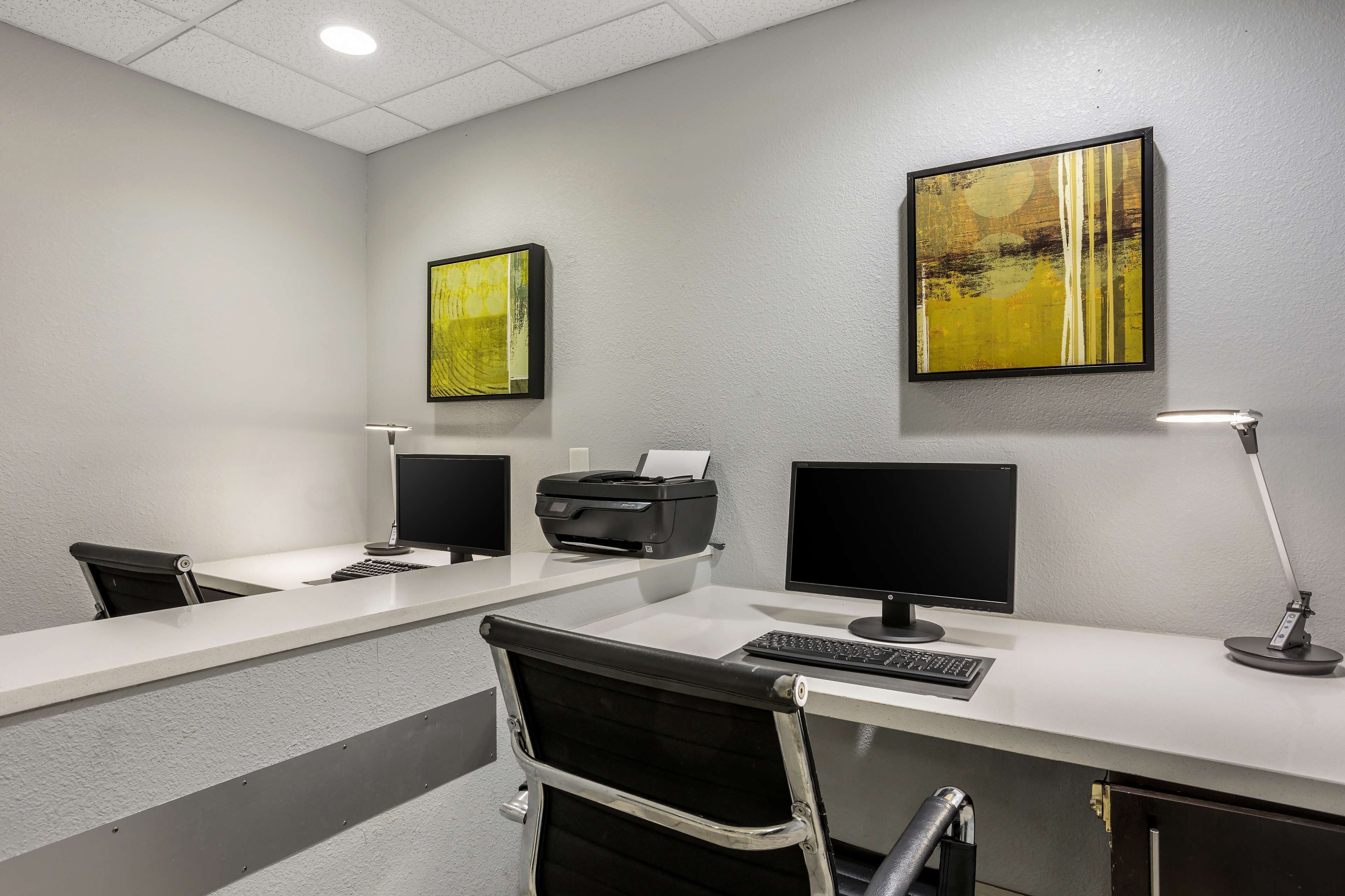 Um espaço de escritório moderno com uma mesa comprida, dois monitores, uma impressora e um teclado.