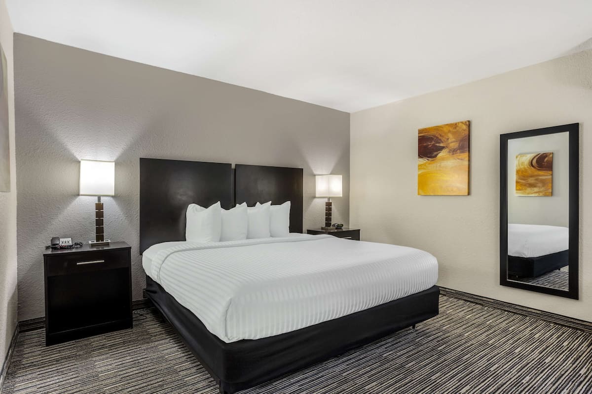 Quarto de hotel com uma cama grande, duas mesas de cabeceira com luminárias, um espelho fixado na parede e arte abstrata.