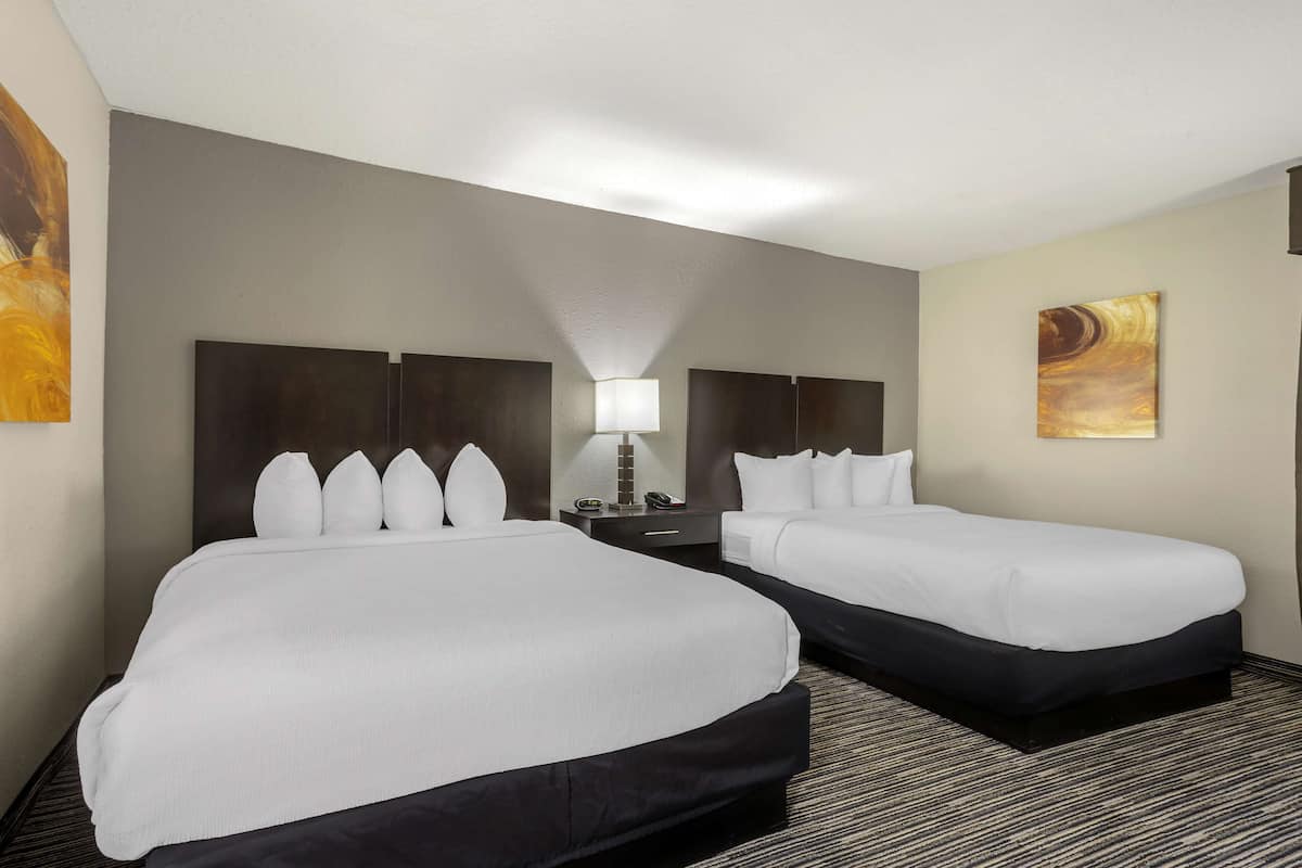 Quarto de hotel com duas camas, uma mesa de cabeceira, uma luminária e obras de arte nas paredes.