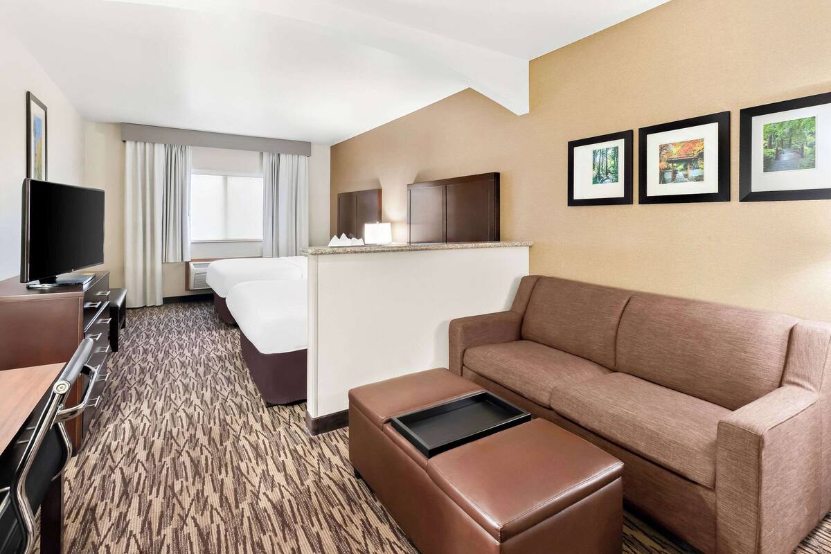 Quarto de hotel com cama, sofá, televisão, escrivaninha e uma mesa pequena.