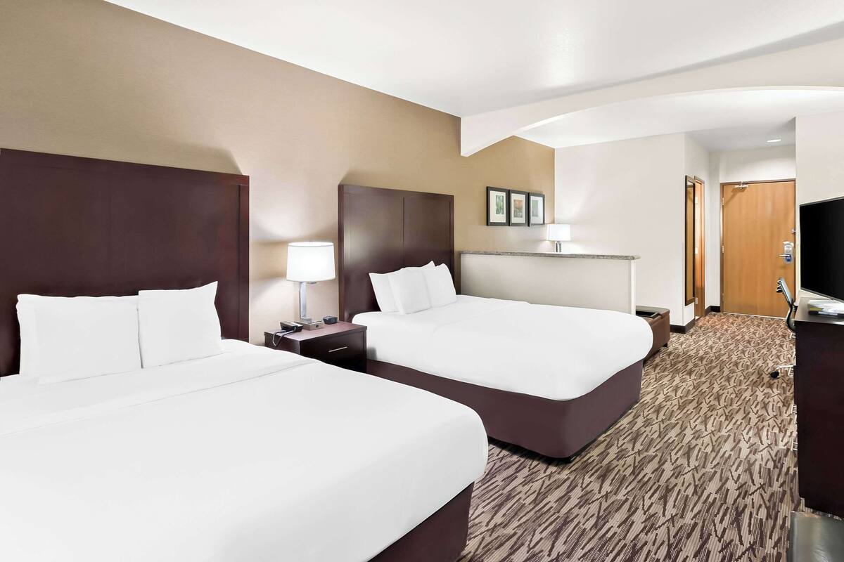Quarto de hotel com duas camas, uma escrivaninha, uma televisão e a porta do banheiro.