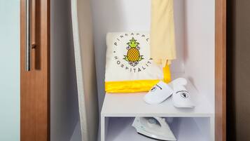 Armário bem arrumado com um cabideiro, um par de chinelos brancos e um painel de passar roupa branco.