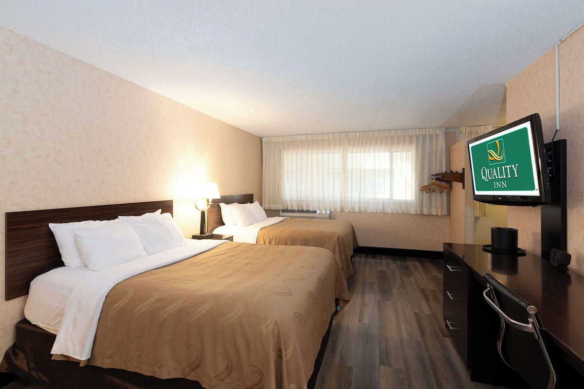 Quarto de hotel com duas camas, televisão, escrivaninha e janela com cortinas.