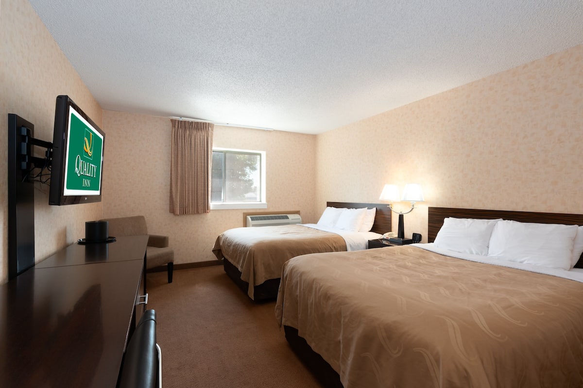 Quarto de hotel com duas camas, uma escrivaninha, televisão e janela com cortinas.