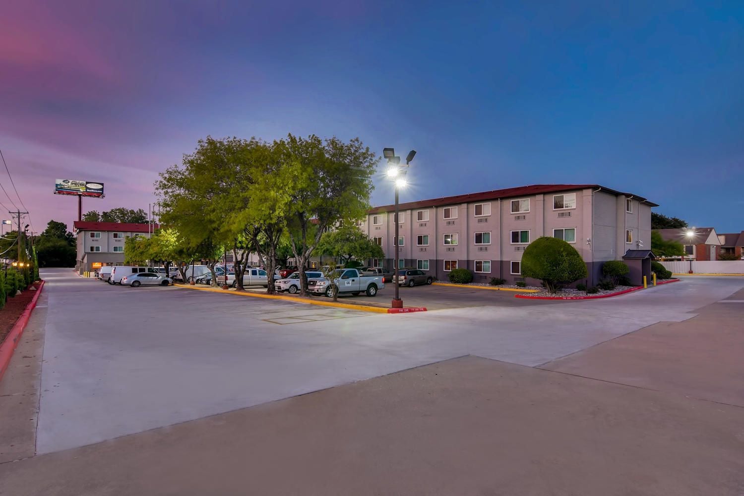 Hotel com estacionamento, árvores e um edifício com várias janelas.