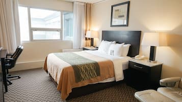 Quarto de hotel com cama, duas mesas de cabeceira com luminárias, escrivaninha com cadeira e janela com cortinas.