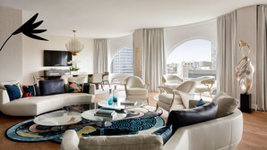 Uma sala de estar moderna com um sofá curvo, uma mesa de centro redonda e vista para a cidade através de grandes janelas.
