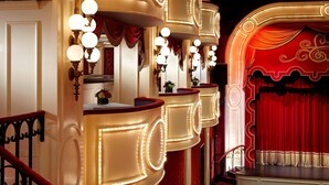 Um teatro com arandelas de parede ornamentadas e iluminadas e um pano de fundo de cortina vermelha.