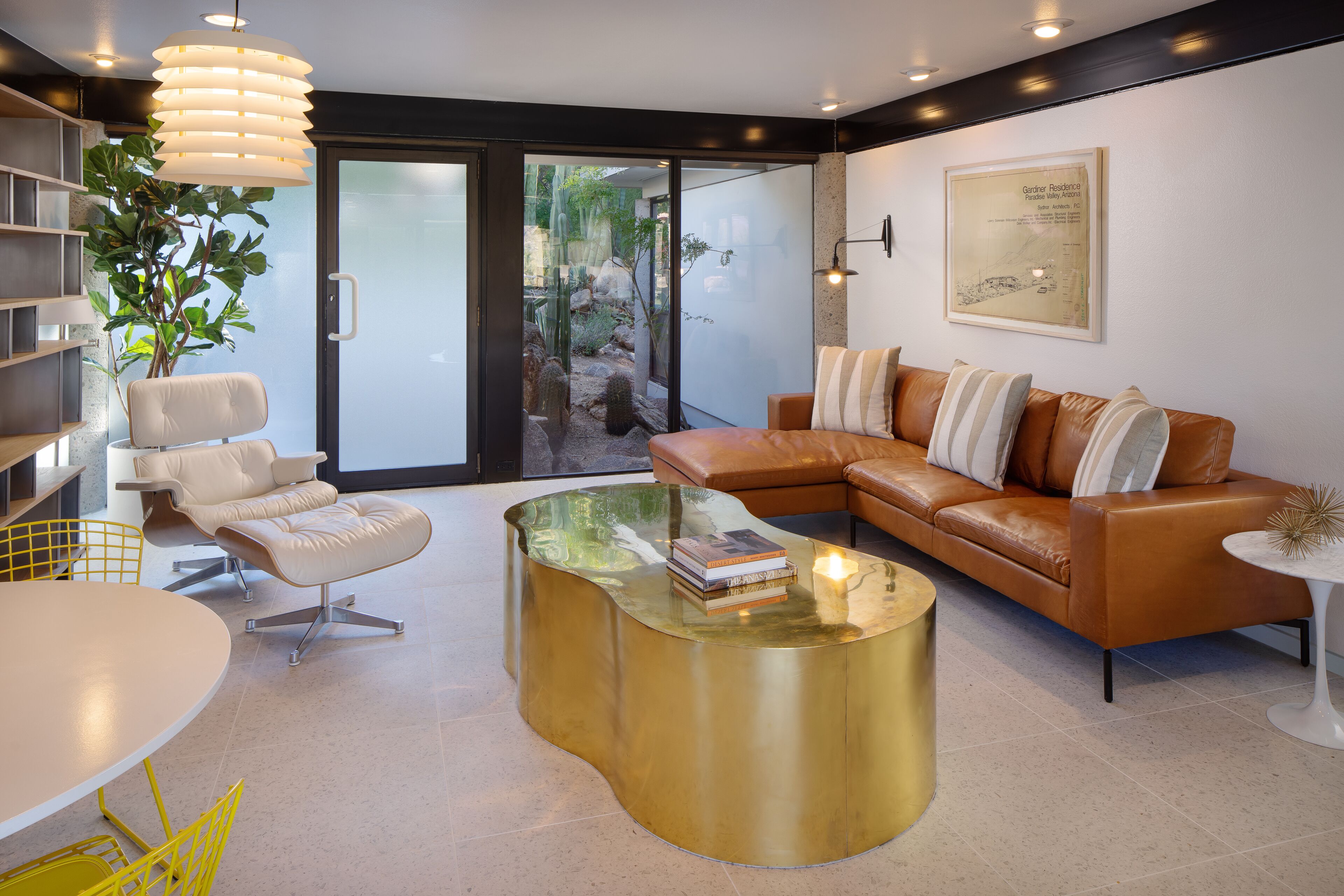 Uma sala de estar moderna com um sofá de couro, uma mesa de centro de vidro e um espaço de jantar com cadeiras amarelas.