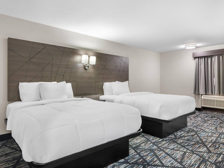 Quarto de hotel com duas camas, uma luminária grande fixada na parede e um tapete estampado.