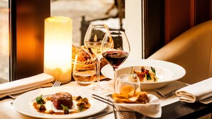 Uma mesa posta com uma vela, copos de vinho, pratos de comida e uma cesta de petiscos.