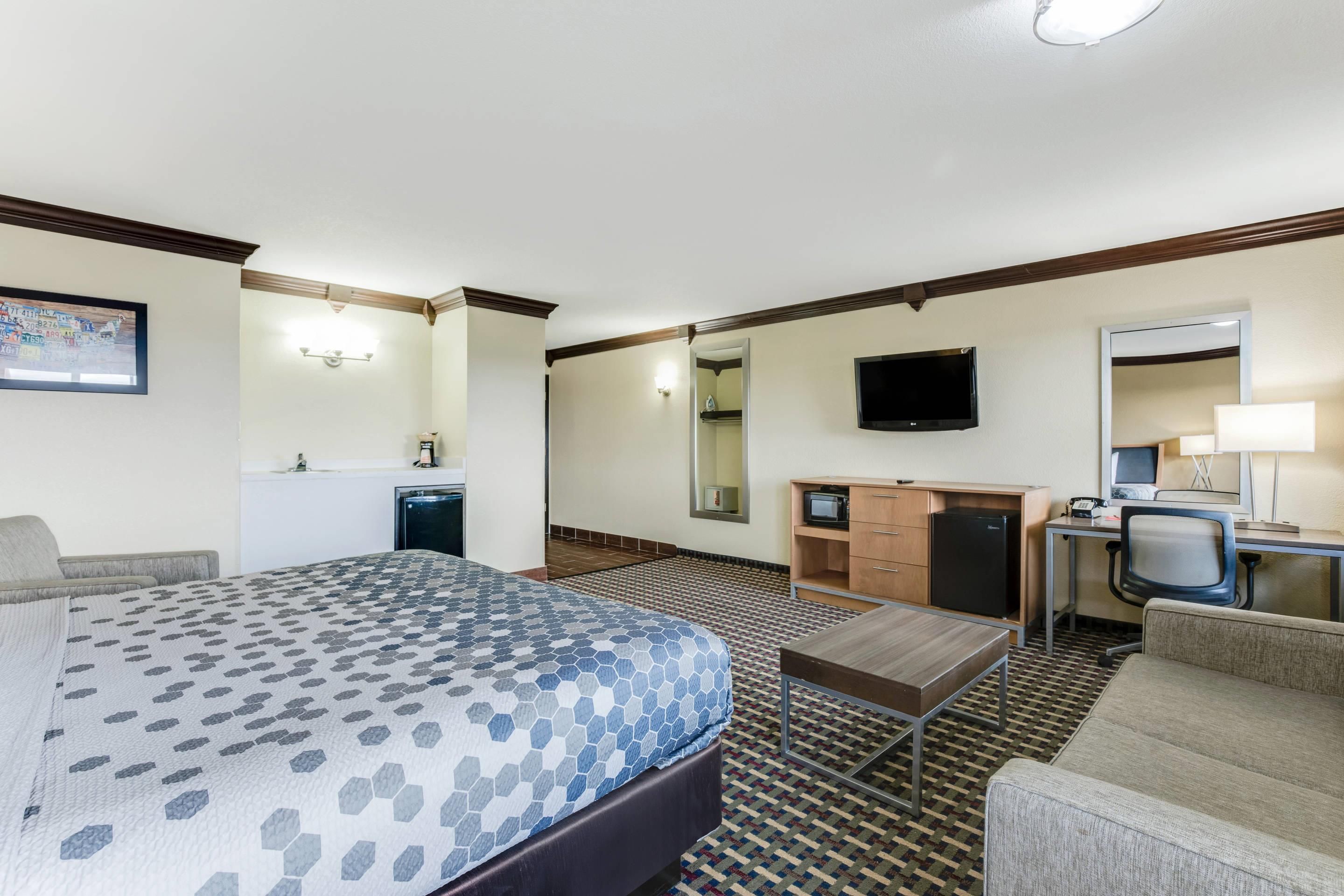 Quarto de hotel com cama, escrivaninha, cadeira, televisão e espelho.