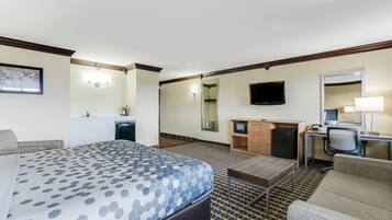 Quarto de hotel com cama, escrivaninha, cadeira, televisão e espelho.