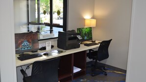 Escritório de hotel com computador de mesa, impressora e luminária.