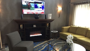 Uma sala de estar com televisão de tela plana, lareira, sofá e mesa de centro.