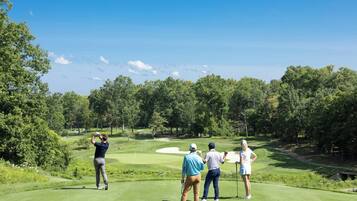 Campo de golfe com céu limpo, árvores e um grupo de pessoas no green.