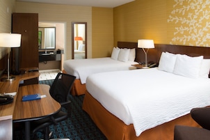 Quarto de hotel com duas camas, uma mesa, uma cadeira, um espelho e banheiro.