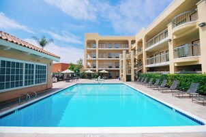Piscina rodeada por espreguiçadeiras e guarda-sóis, com um edifício ao fundo com a inscrição 'POOL SIDE'.