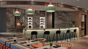 Um restaurante moderno com área de bar, assentos com almofadas e iluminação pendente.