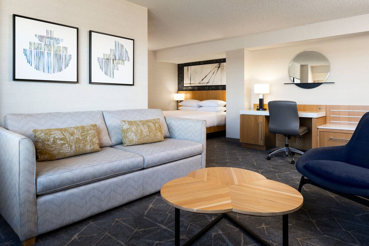 Quarto de hotel com sofá, cama, escrivaninha, cadeira e duas obras de arte emolduradas na parede.