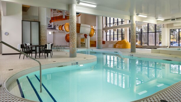 Uma piscina interna com piso revestido, área de estar com cadeiras e um escorregador.