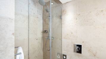 Uma casa de banho moderna com chuveiro em cabine de vidro, um porta-toalhas e um painel de controlo fixado na parede.
