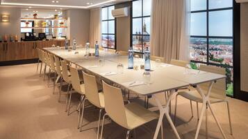 Sala de conferências com uma mesa comprida, cadeiras e vista da cidade através de grandes janelas.