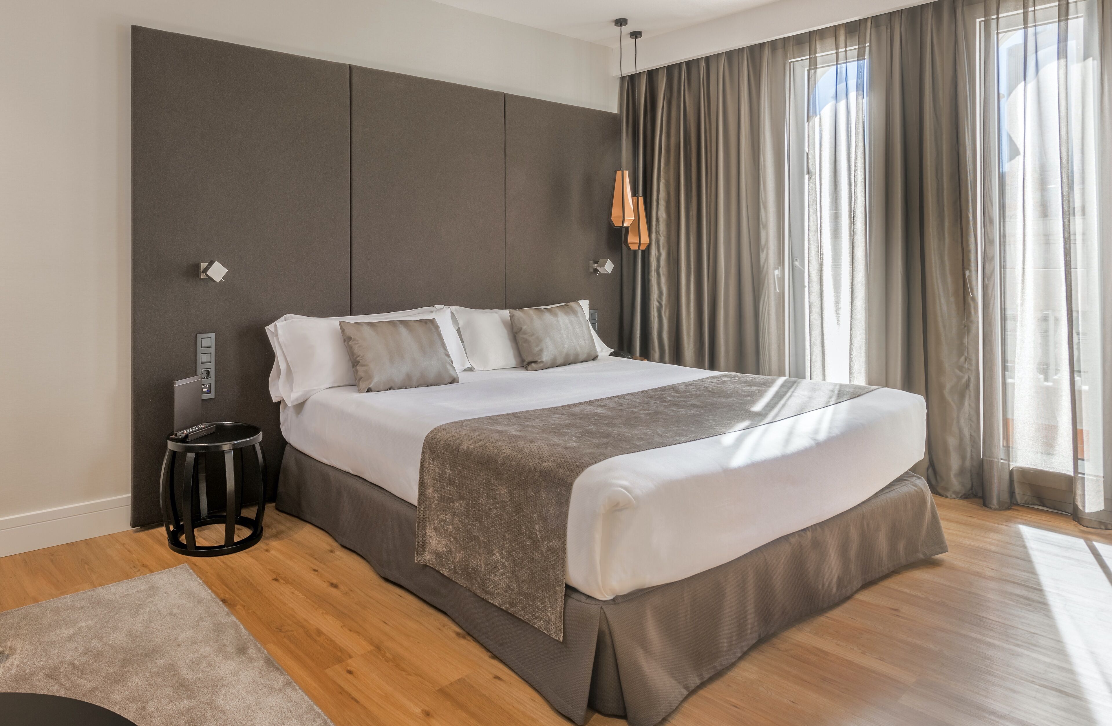 Quarto moderno com uma cama grande, mesa de cabeceira e janela com cortinas.