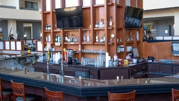 Uma área de bar com balcão, banquetas e prateleiras cheias de garrafas e copos.