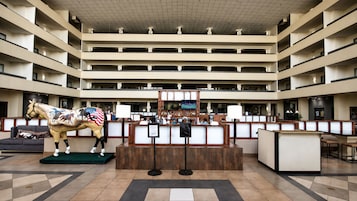 Um hall de hotel com vários níveis, uma mesa de recepção, uma estátua de cavalo e uma tela de televisão.