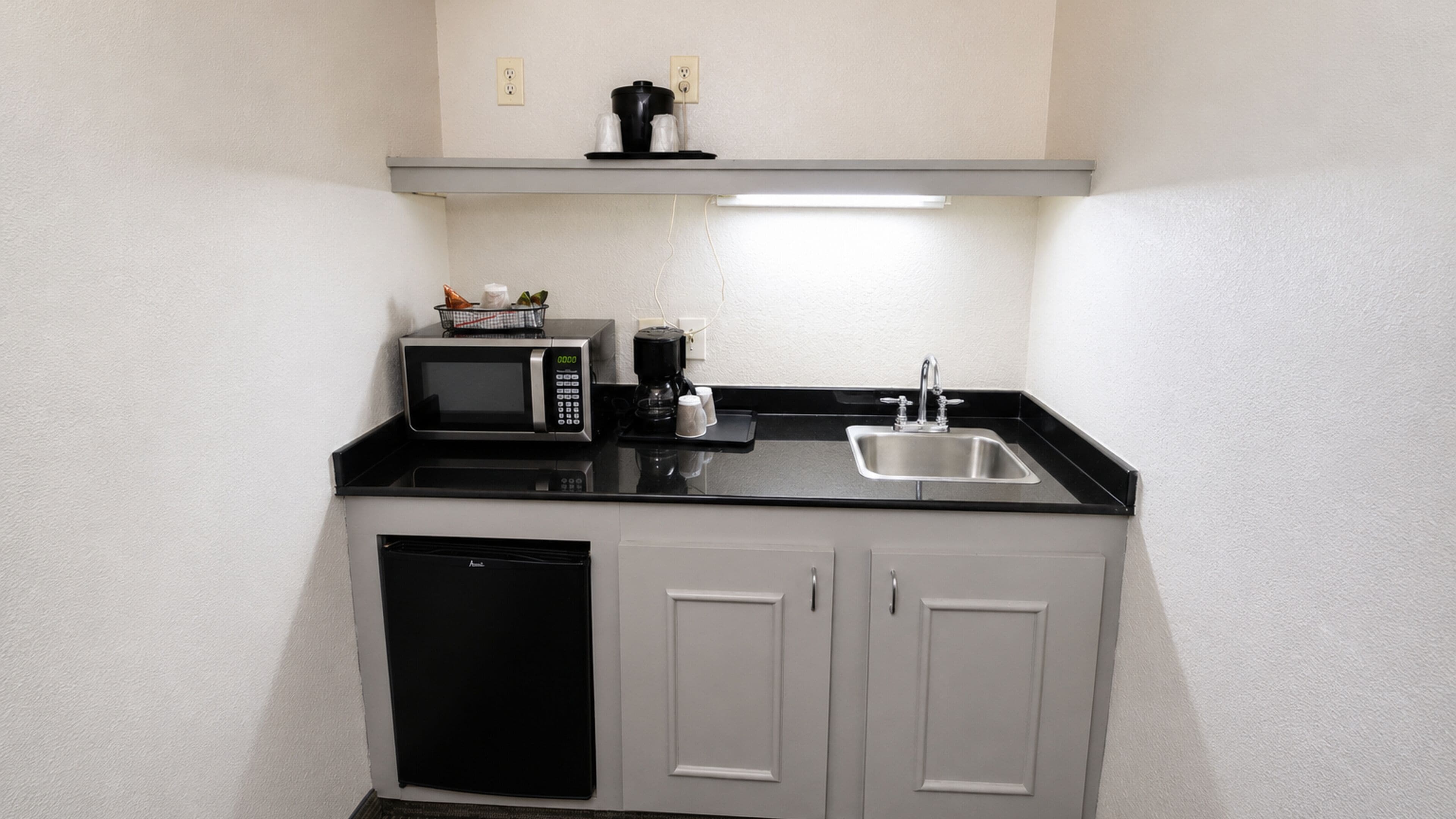 Uma cozinha compacta equipada com micro-ondas, cafeteira e pia.