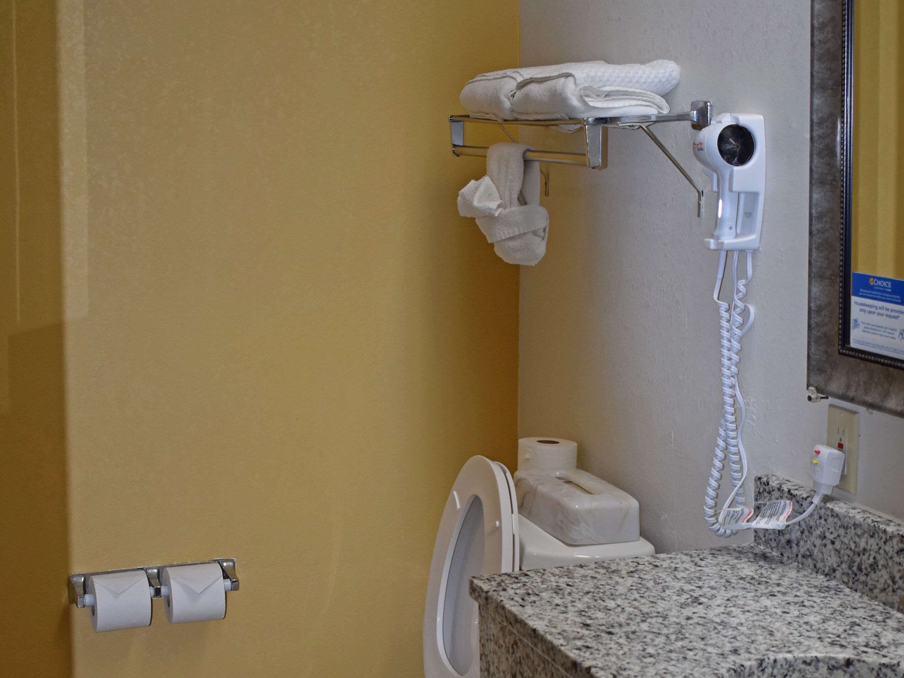 Um banheiro com bancada de mármore, porta-toalhas com toalhas, secador de cabelo, suporte para papel higiênico e secador de mãos.