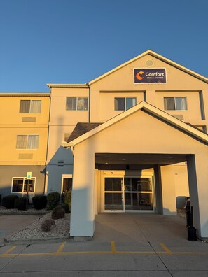 Edifício do Comfort Inn & Suites com entrada coberta, placa de estacionamento para deficientes e céu limpo.