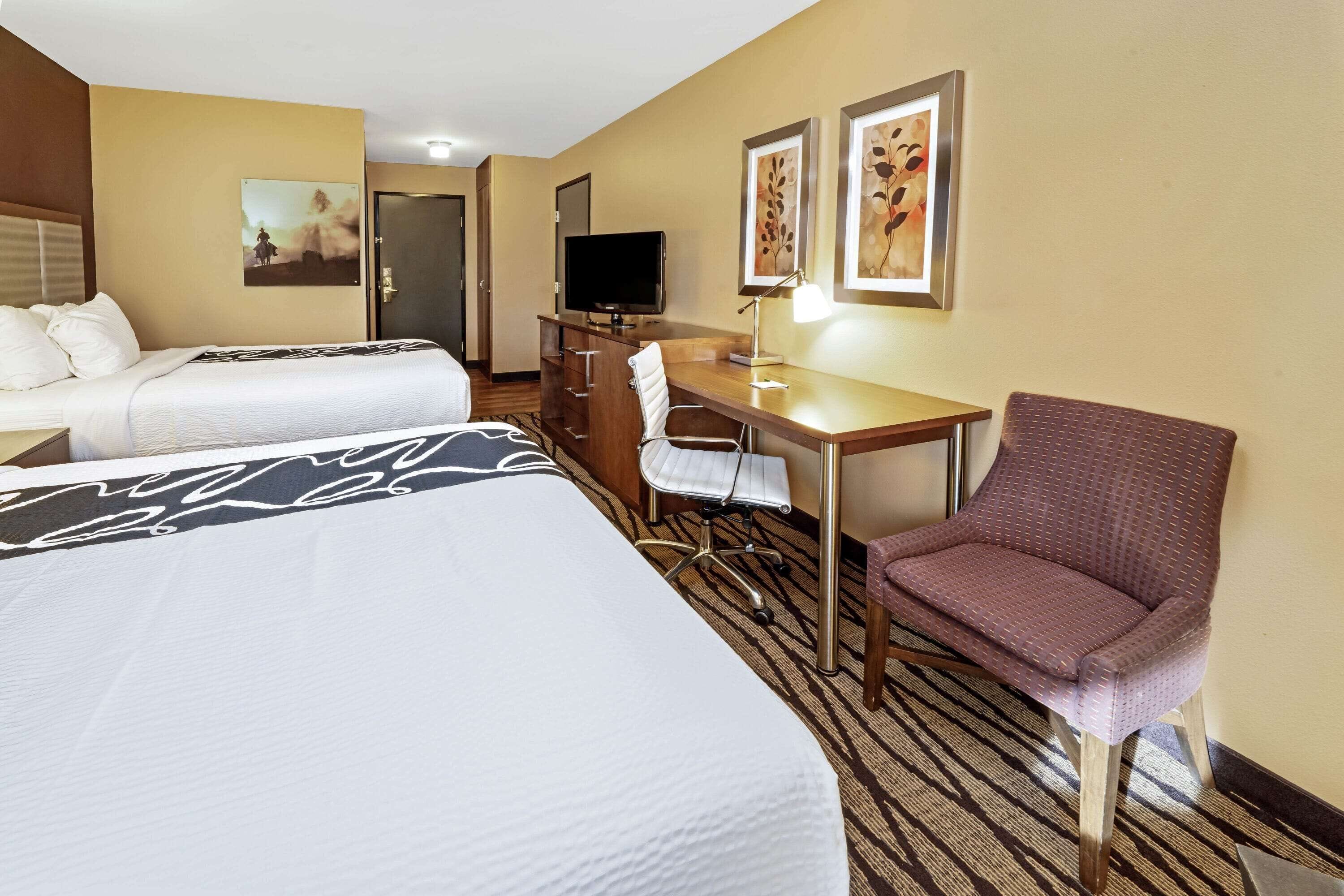 Quarto de hotel com duas camas, uma escrivaninha, uma cadeira, televisão e obras de arte nas paredes.