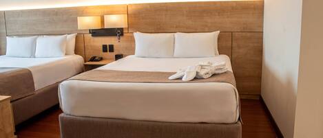 Quarto de hotel com duas camas, mesa de cabeceira com telefone e um par de chinelos brancos na cama.