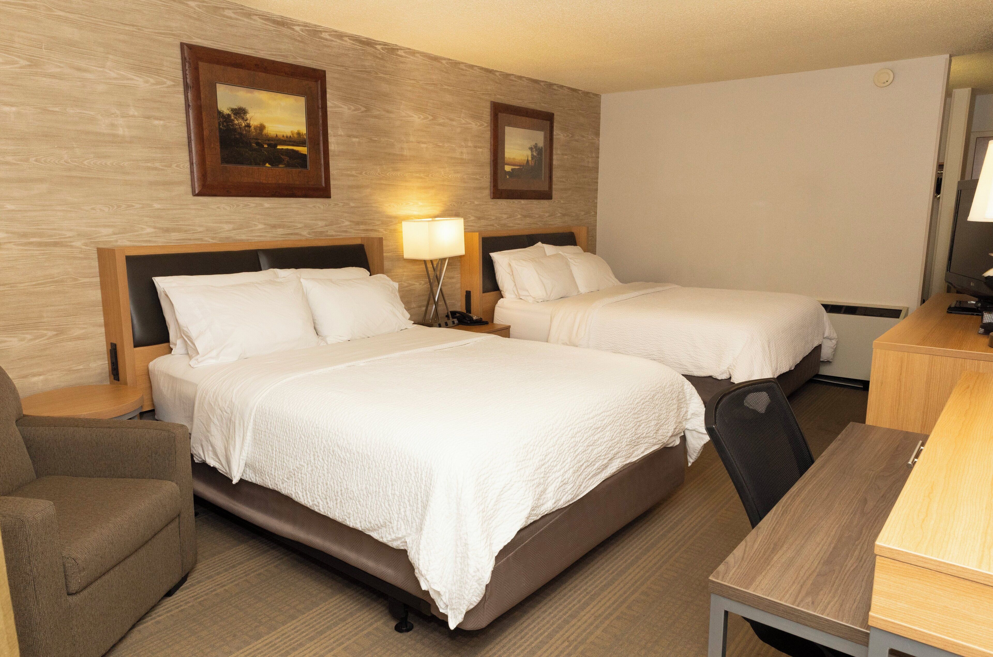 Quarto de hotel com duas camas, uma escrivaninha, uma cadeira e duas mesas de cabeceira com abajures.