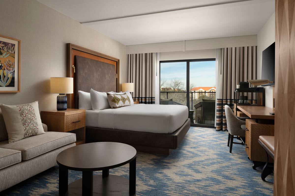 Quarto de hotel com uma cama grande, um sofá, uma escrivaninha e varanda com vista.