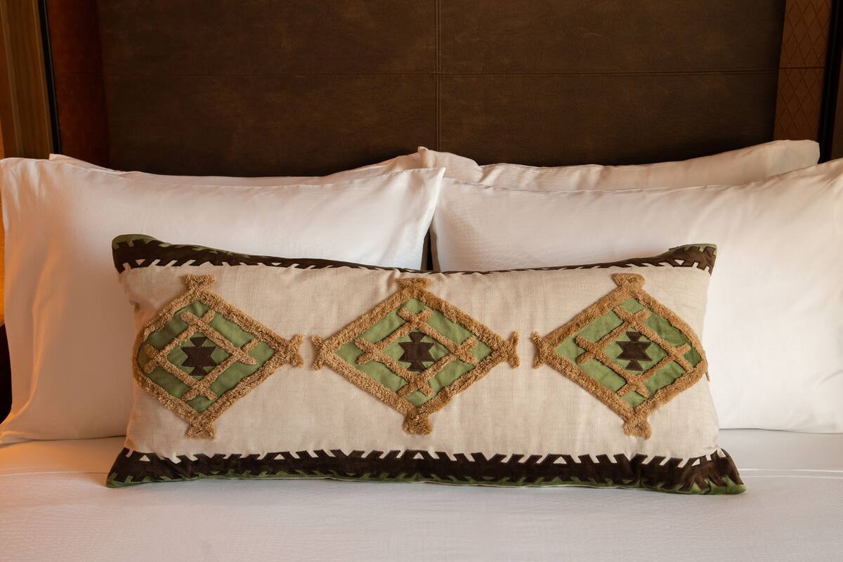 Uma cama com dois travesseiros, um liso e outro com padrão geométrico.