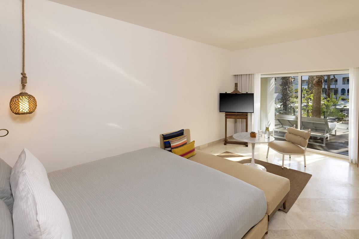 Quarto de hotel moderno com cama, televisão, mesa pequena e varanda com vista.