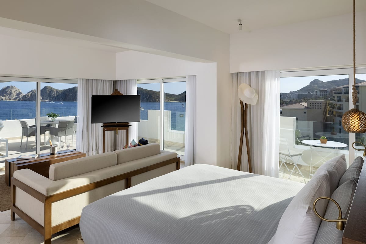 Um quarto espaçoso com uma cama grande, televisão de tela plana e varanda vista para o mar.