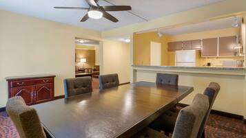 Sala de conferências com uma mesa grande, seis cadeiras, um ventilador de teto e uma kitchenette ao fundo.